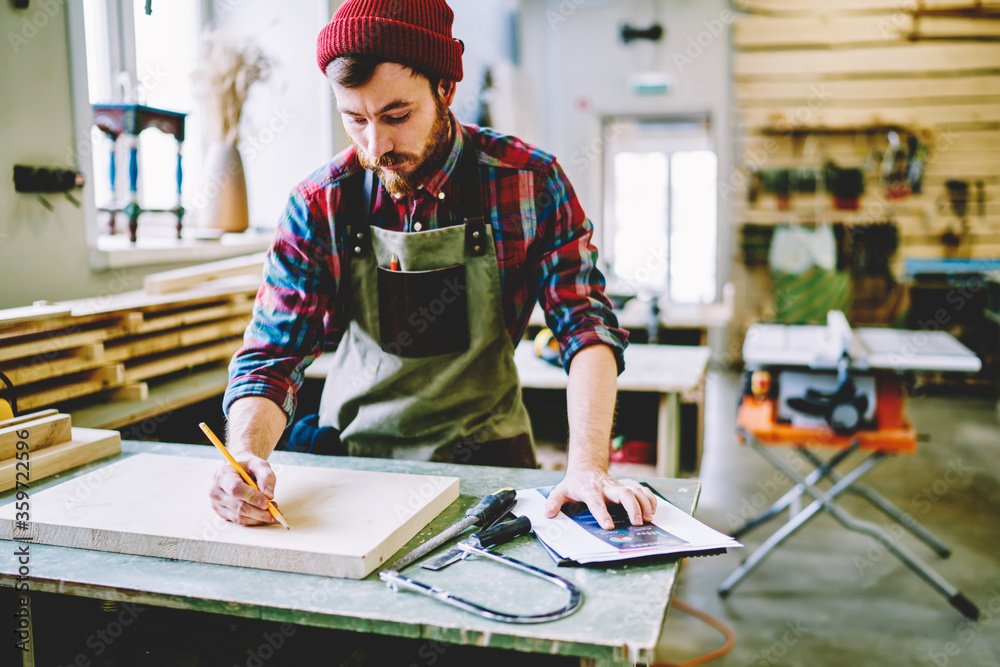 Foto de Pensive skilled caucasian male carpenter making drawings on ...