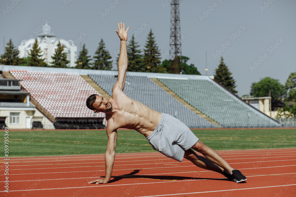 Shirtless muscular man doing a side plank exercise at the stadium ...