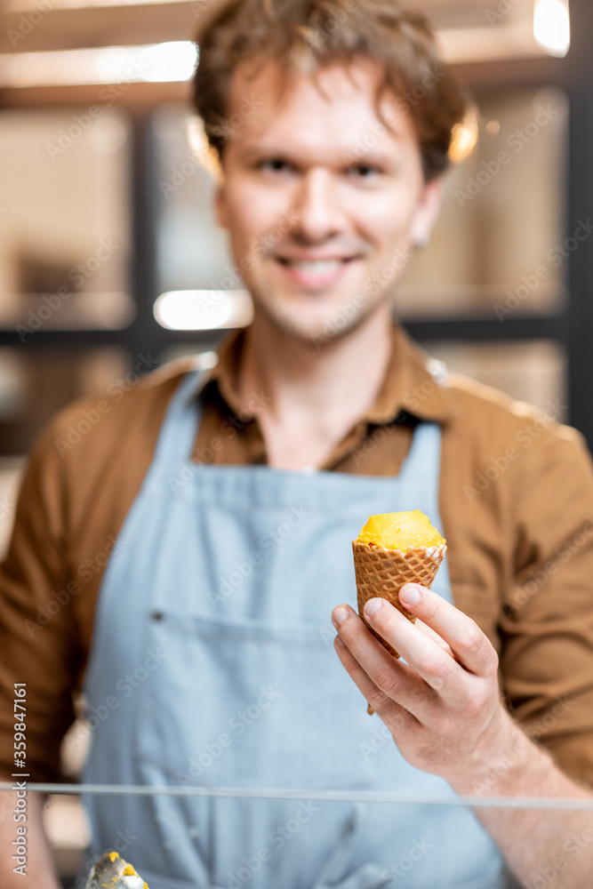 Portrait of a cheerful ice cream seller in working uniform holding ice ...