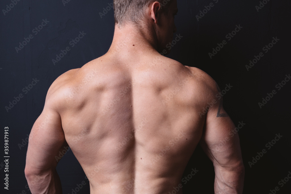 young bodybuilder with a short haircut stands near a black wall ...