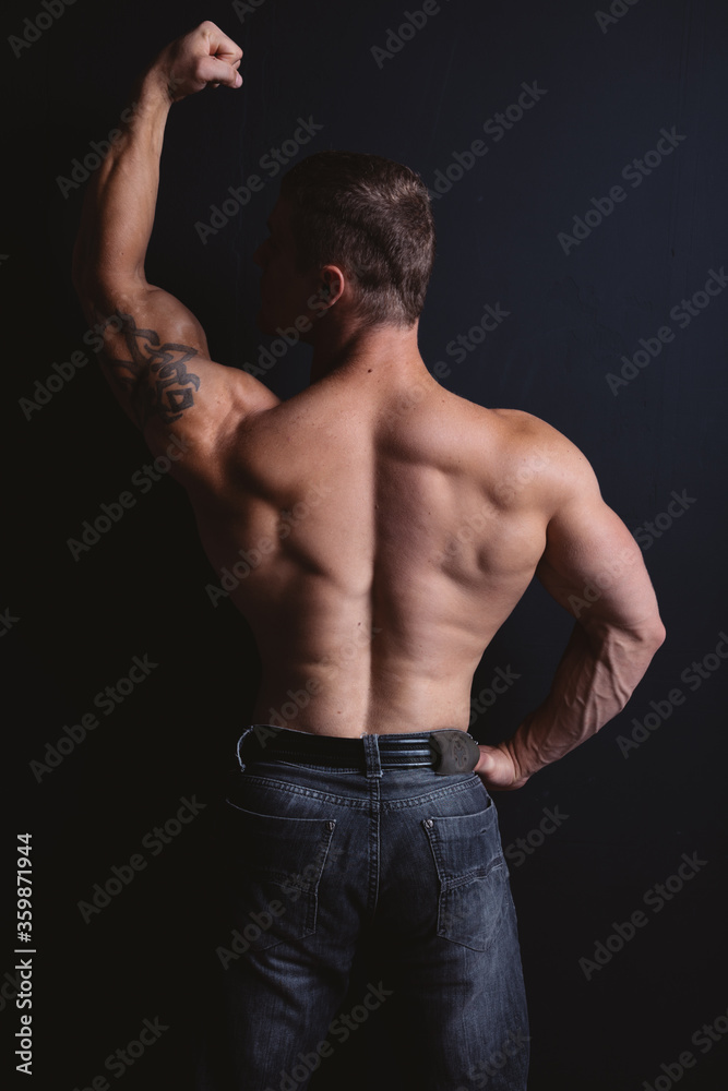 young bodybuilder with a short haircut stands near a black wall ...