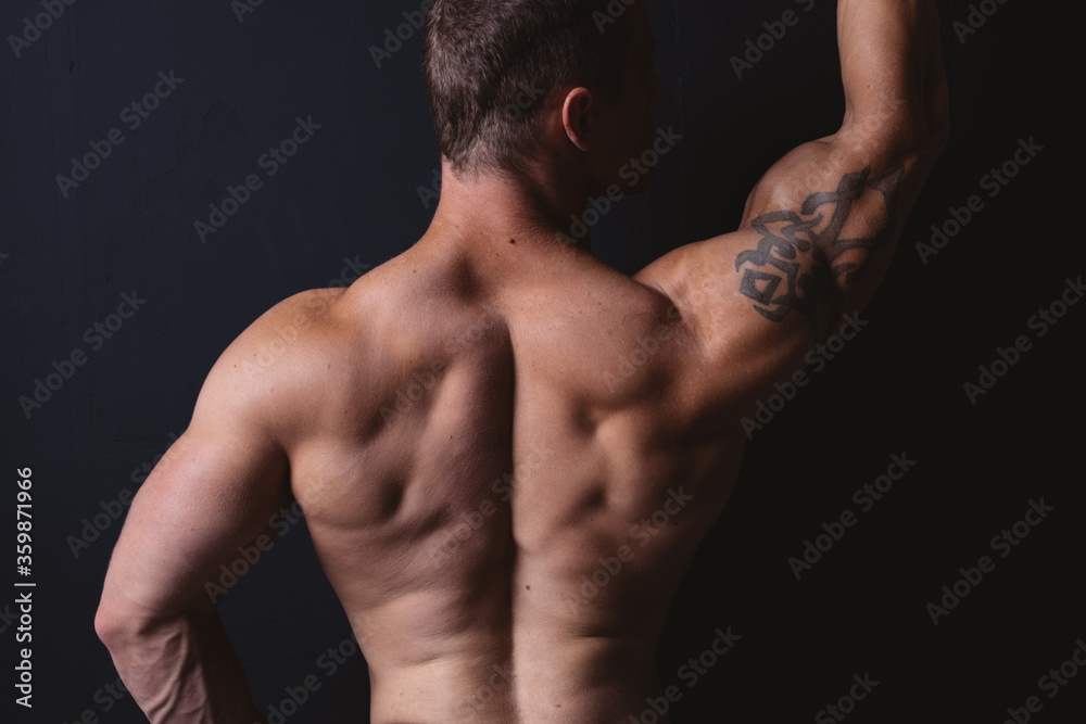 young bodybuilder with a short haircut stands near a black wall ...