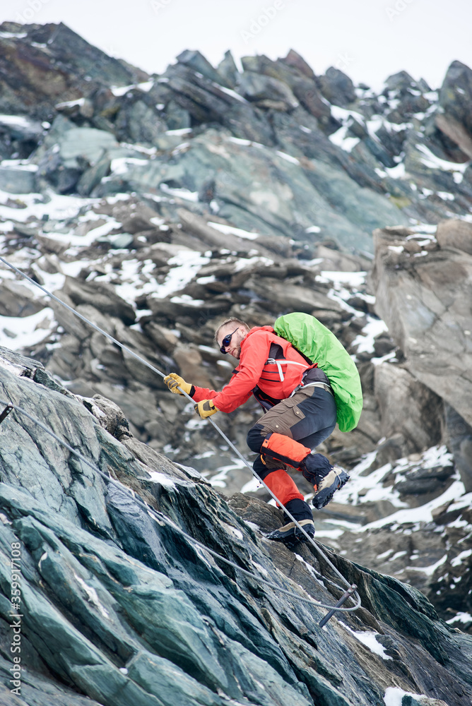 Side view of brave mountaineer in sunglasses holding rope while ...