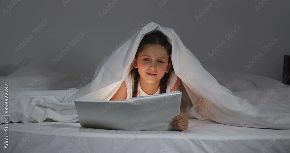 Cute girl with long hair braided in braids reading a book while lying ...