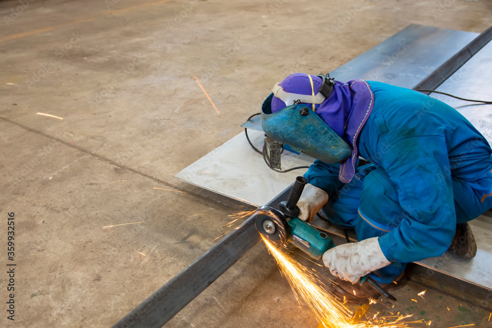 worker in blue uniform cutting metal sheets with electric grinder in ...
