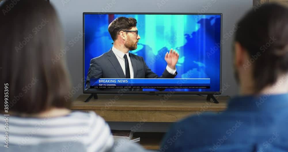 Rear of Caucasian couple sitting on couch and watching TV news in ...
