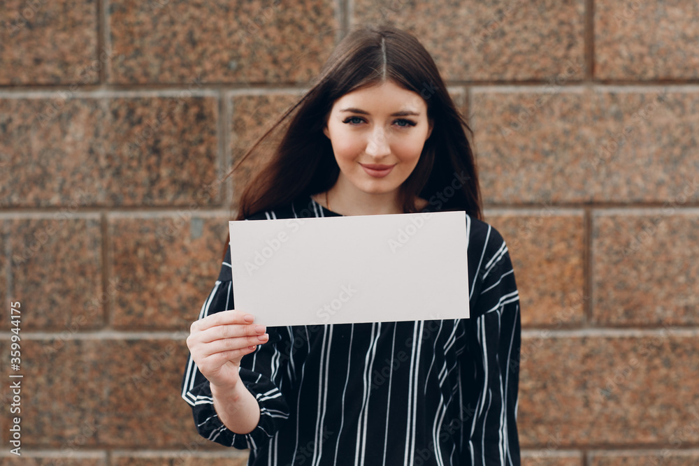 Young woman with smile holds white paper in hand stone background. Girl ...