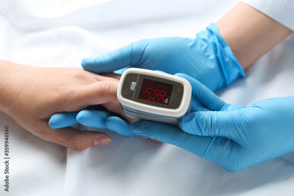 Doctor examining patient with fingertip pulse oximeter in bed, closeup ...