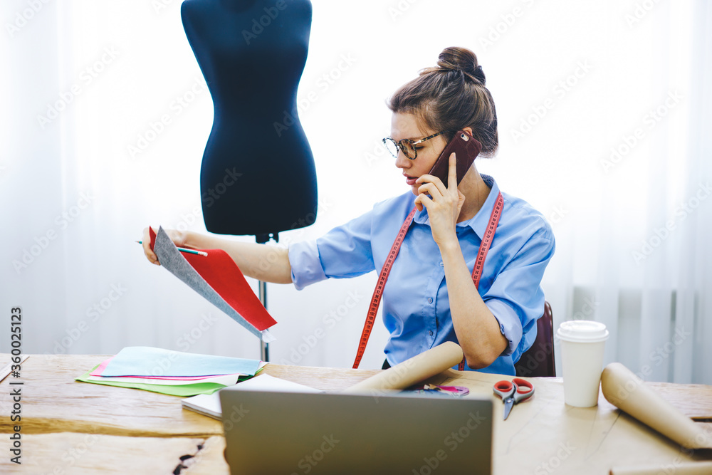 Pondering attractive female designer having mobile conversation on ...