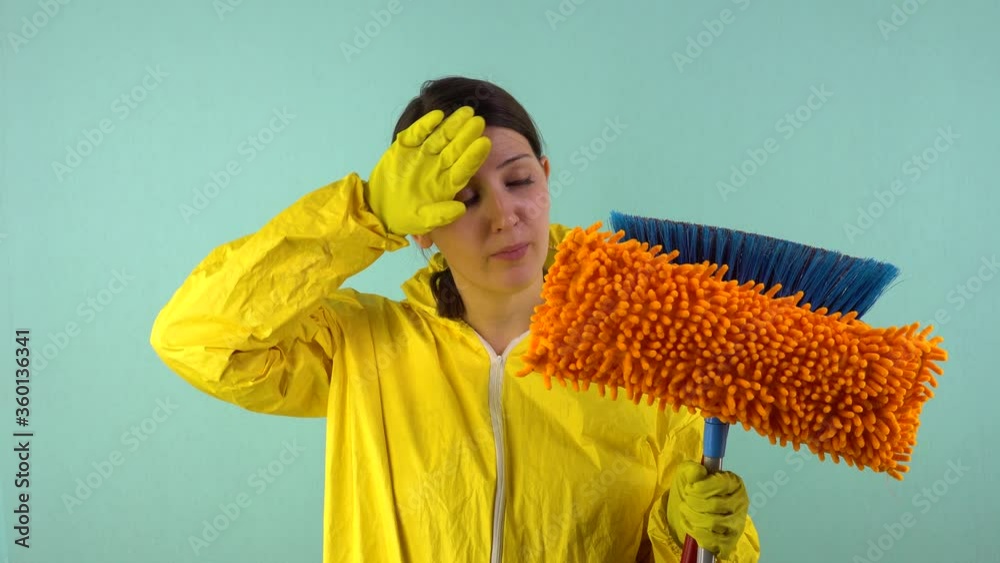 Sad and tired cleaning lady in a yellow suit on a blue background. The concept of professional ...