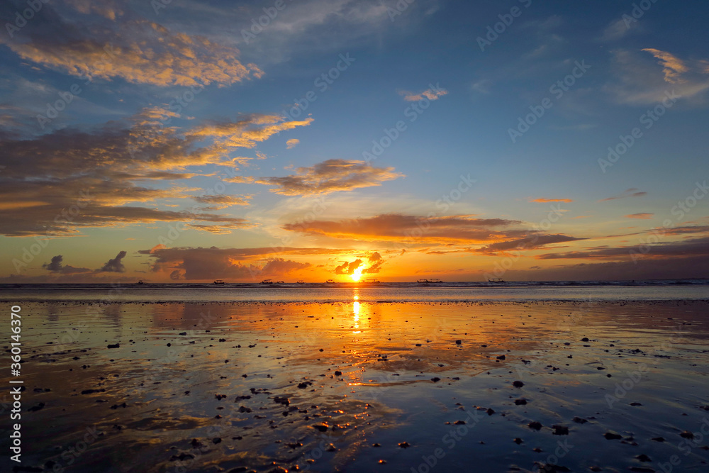 Beautiful Kuta beach sunset with clouds, rocks on sand and reflection ...