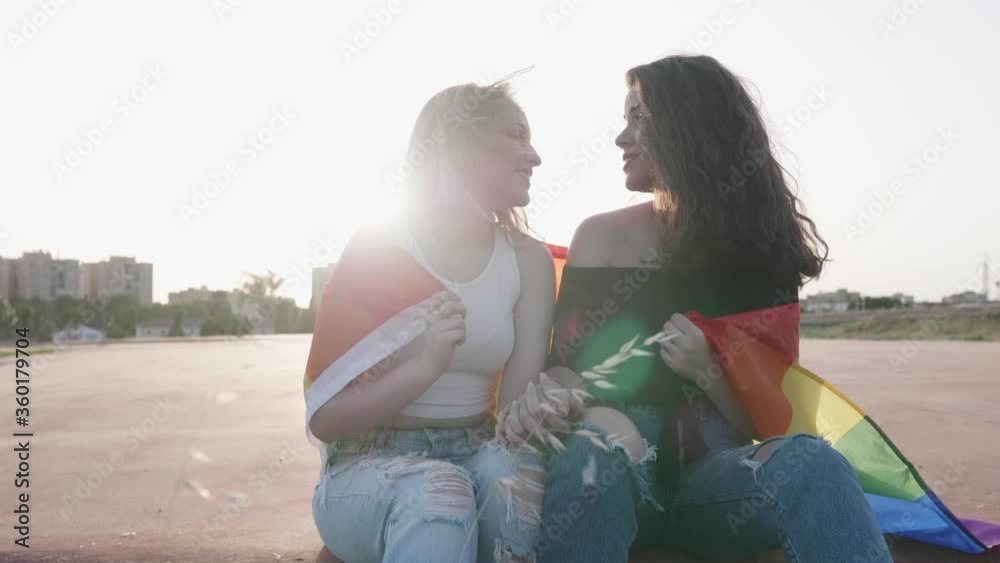 two young girls sitting holding hands and laughing with the LGBT flag ...