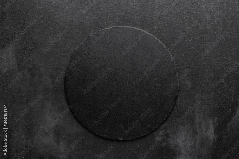 Round black slate stone plate in the middle of a dark grunge scratched ...