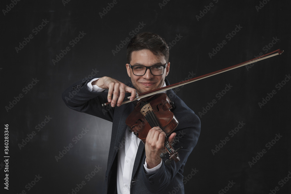 Confident smiling young man playing violin while standing against black ...