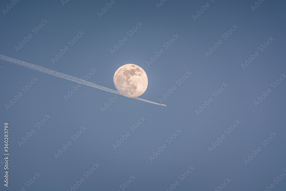 Foto de Airplane leaves a trail while passing a full moon on a clear ...