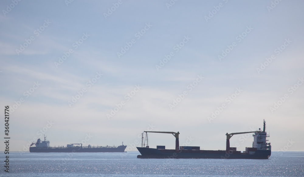 Two cargo ships drifting over the ocean in front of a wispy blue sky ...