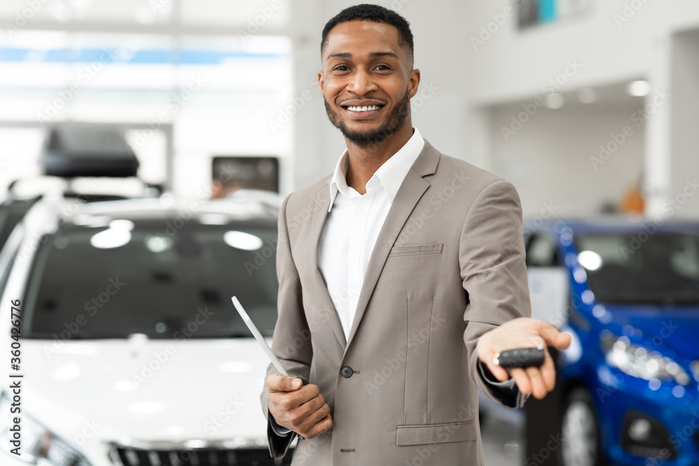 Car Dealer Offering Automobile Key To Camera Standing In Dealership ...