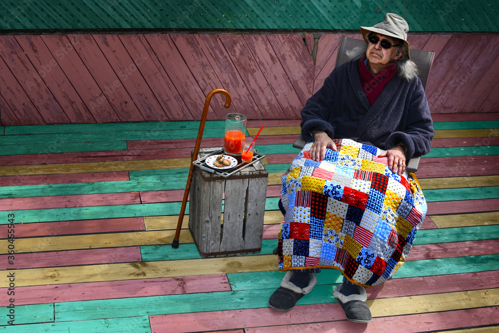 Old man taking the sun on a porch, with a hat, having a snack, sitting ...
