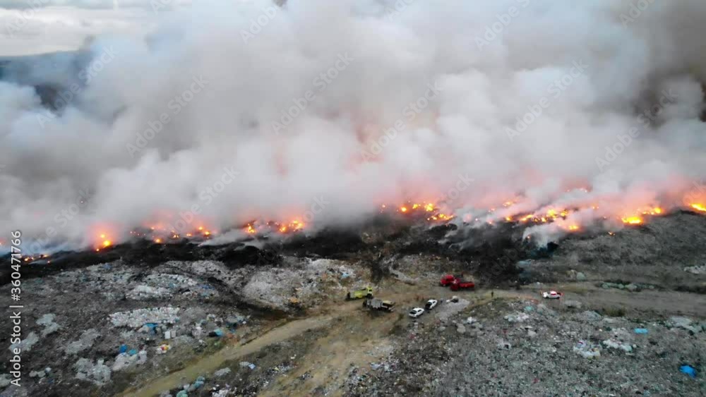 Aerial, reverse, drone shot of a Junkyard on fire, firefighter trucks ...