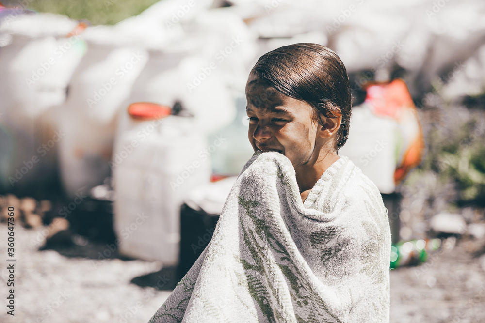 homeless child shrouded in a dirty towel on the background of garbage ...