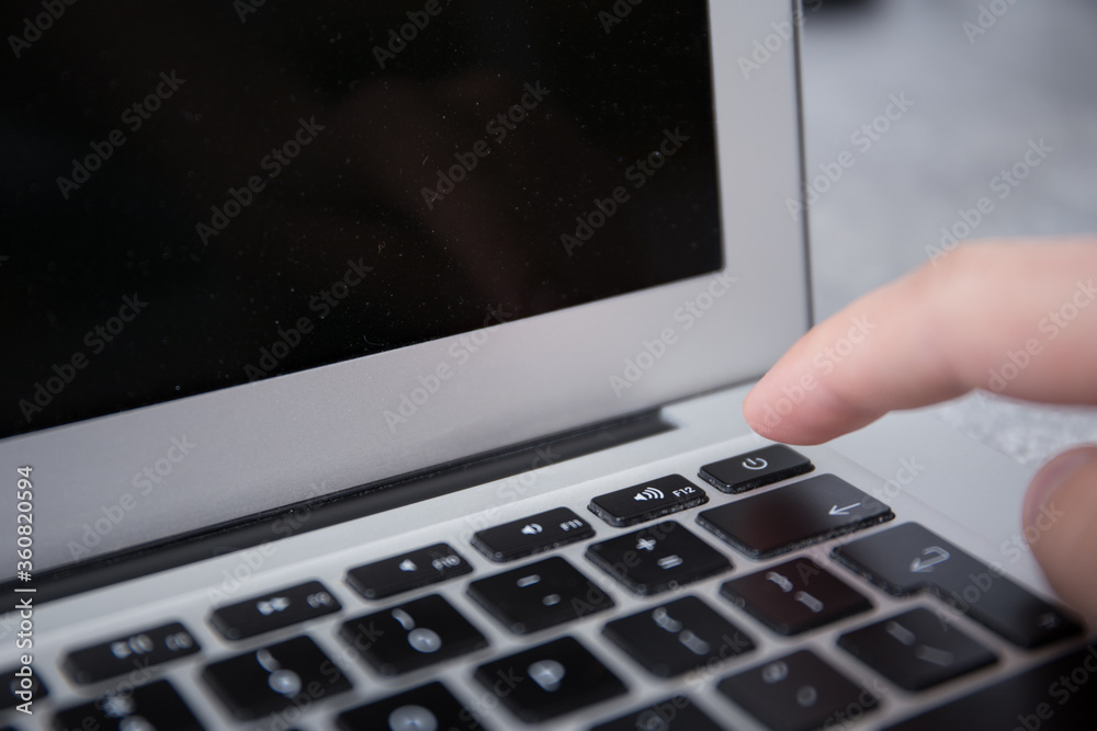 Pushing the power switch on a keyboard of a grey notebook with a finger ...