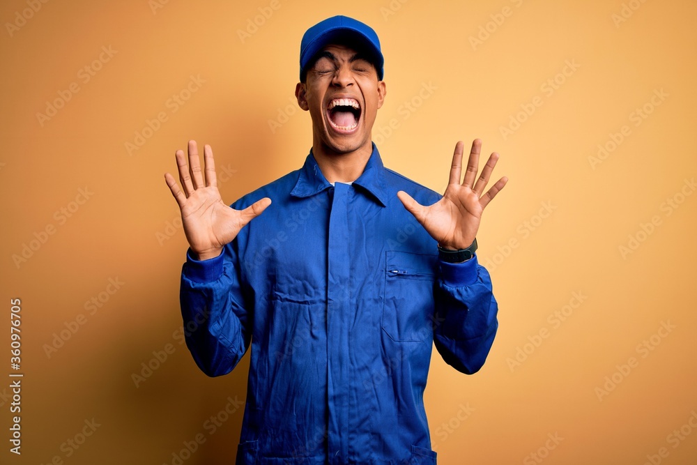 Young african american mechanic man wearing blue uniform and cap over ...