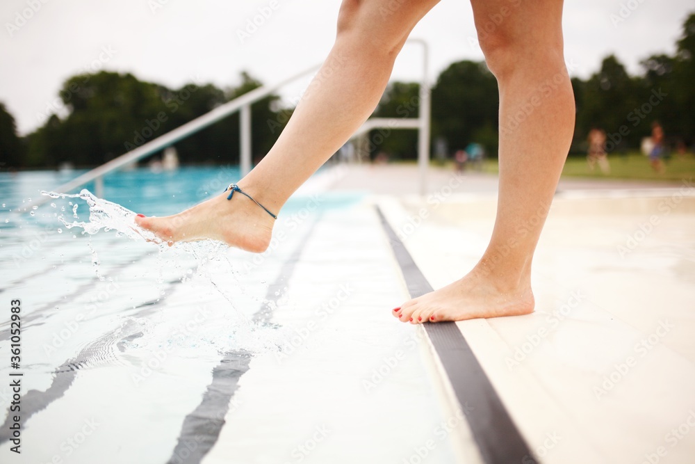 Young adult woman's feet by the pool, checking the water temperature ...