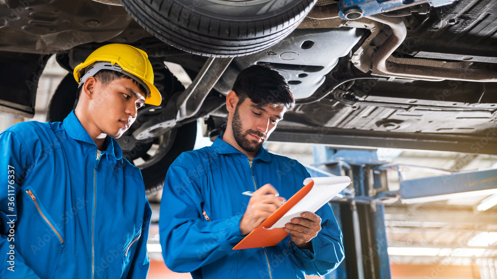 Mechanic in blue work wear uniform inspects the car bottom with his ...
