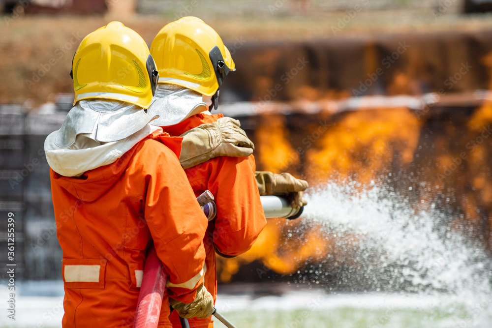 Two brave firefighter in fire suit on rescue duty using water from hose ...