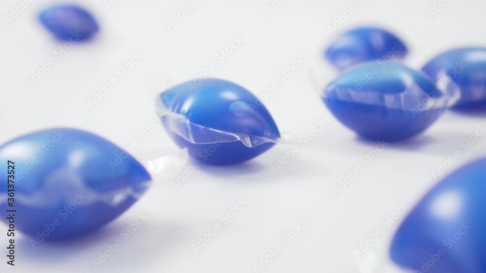 Close-up of pods with blue detergent falling on a white background ...