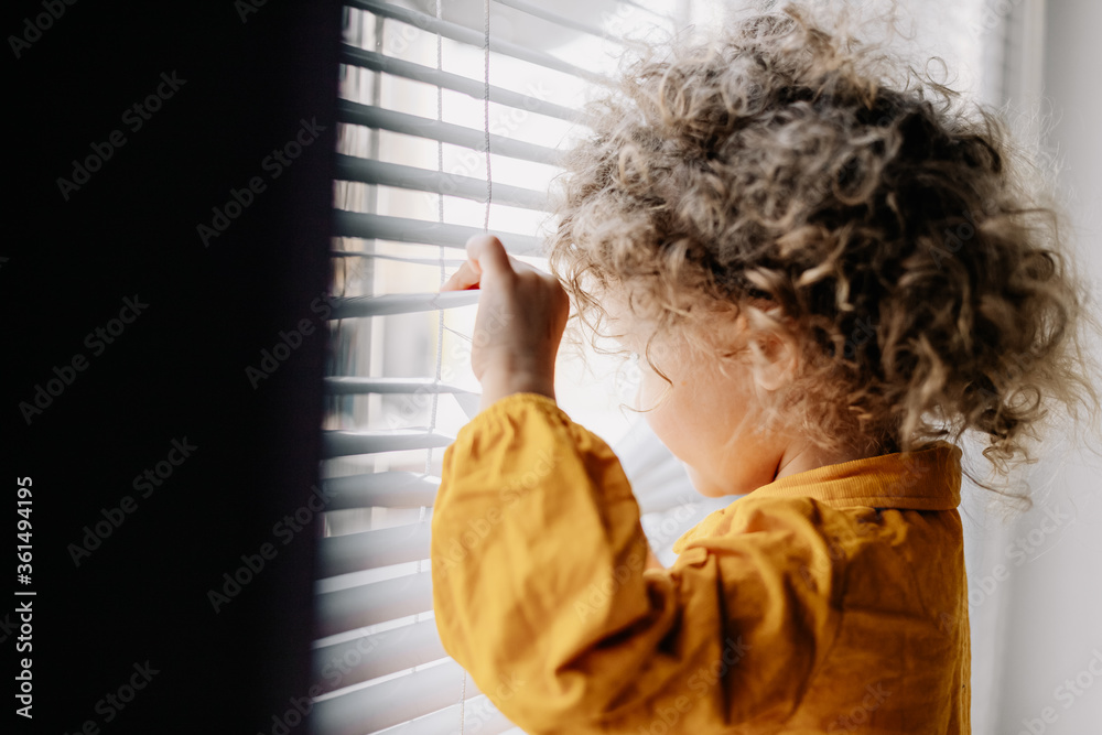 The child opens the blinds with his hands and looks out the window ...