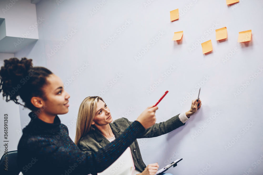 Foto de Two female colleagues pointing on stickers with creative ideas ...