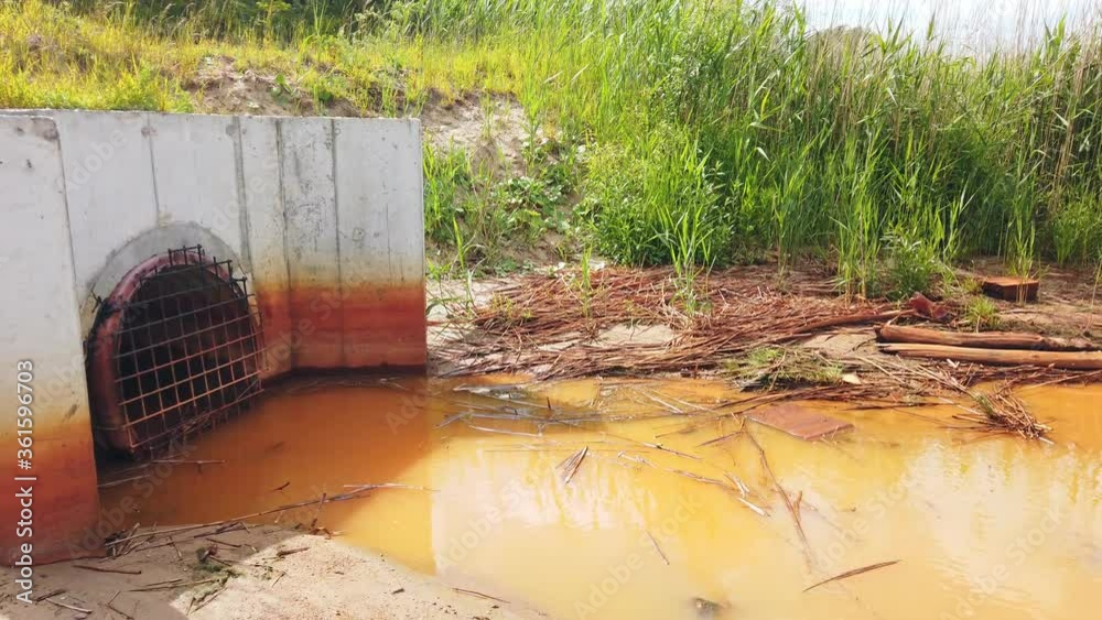 Sewer or drain pipe pollutes city river with rusty brown wastewater in ...