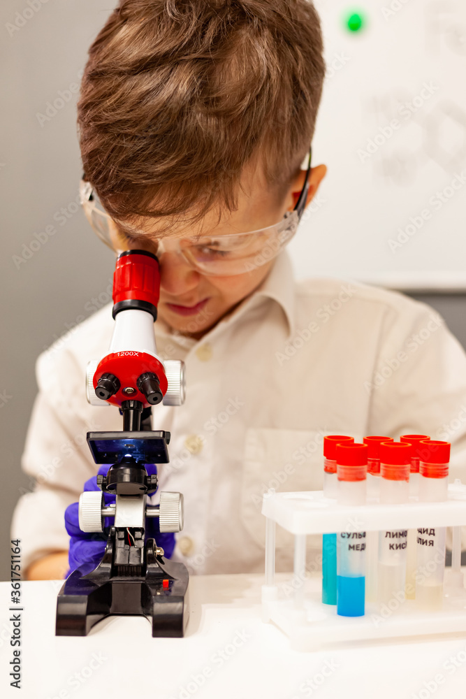 boy in laboratory gloves and goggles plays with laboratory test tubes ...