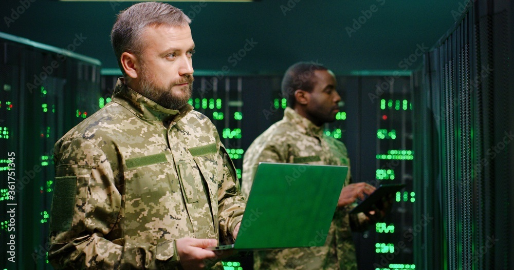Caucasian military male officer in camouflage standing in server room ...