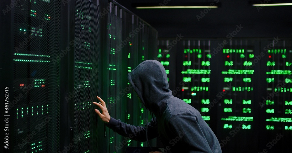 Male Asian guy data thief in dark hood stealing in the server room with ...