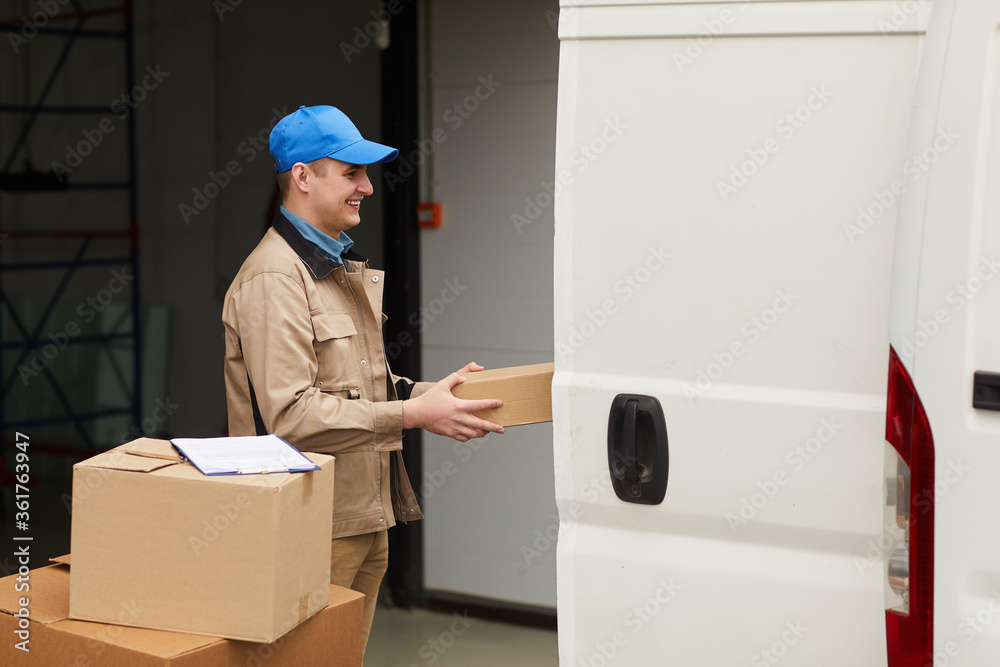 Manual worker carrying boxes and loading them into the van in warehouse ...
