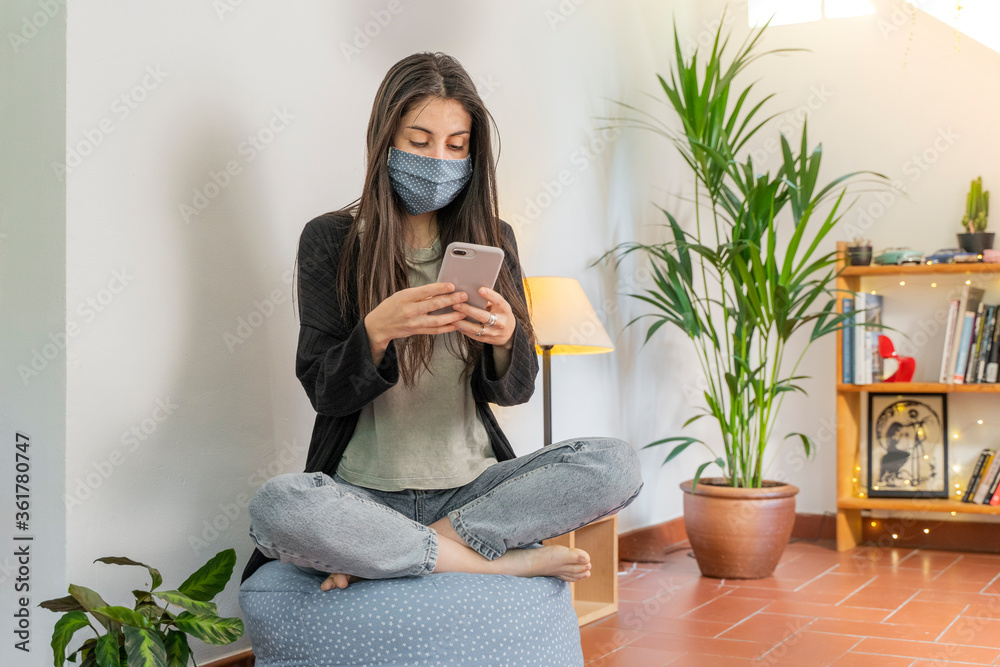 Coronavirus. Woman sitting down using mobile phone. Wearing mask ...