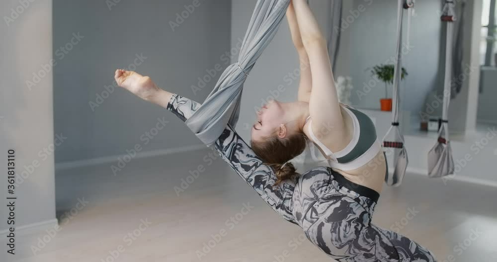 Young gymnast woman stretches herself and spins on the yoga hammok in ...