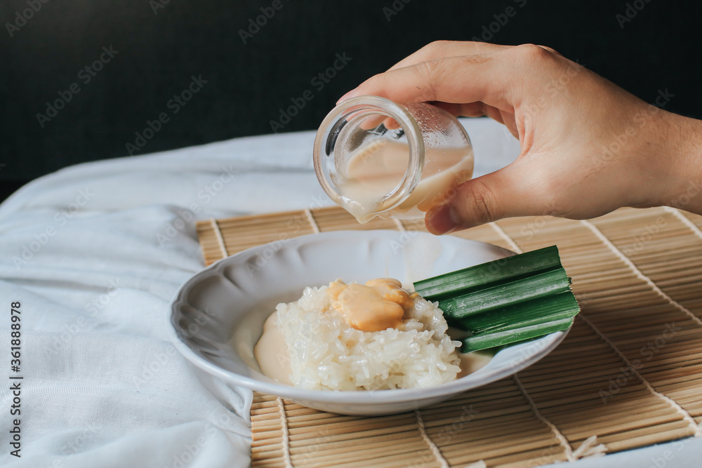 Hand pouring coconut milk durian creamy sauce in Thai sweet sticky rice ...