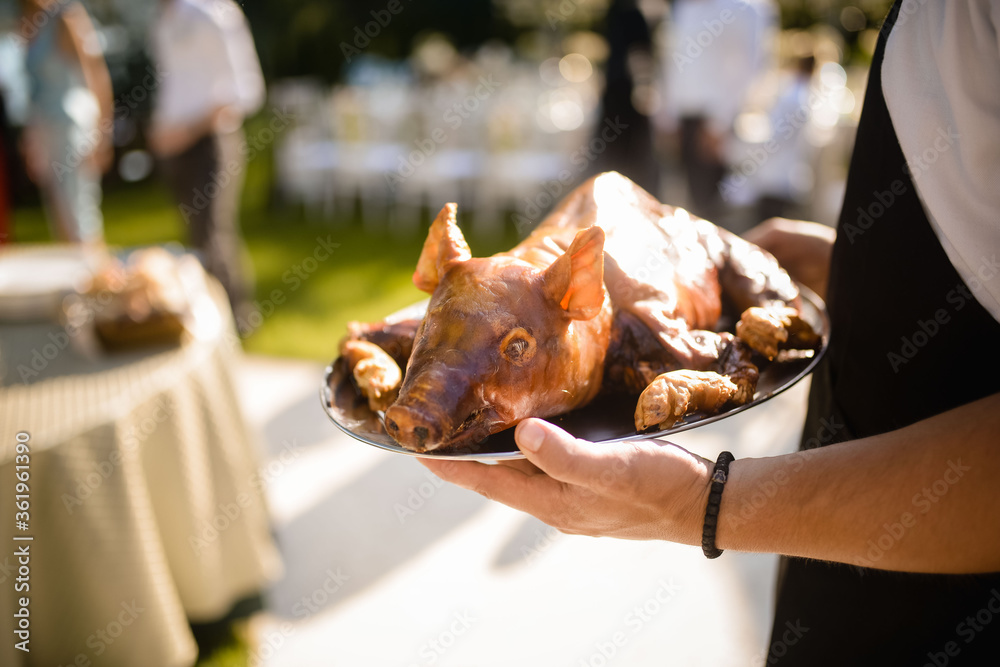 The waiter serves the roast pig on an oval at an outdoor party Stock ...