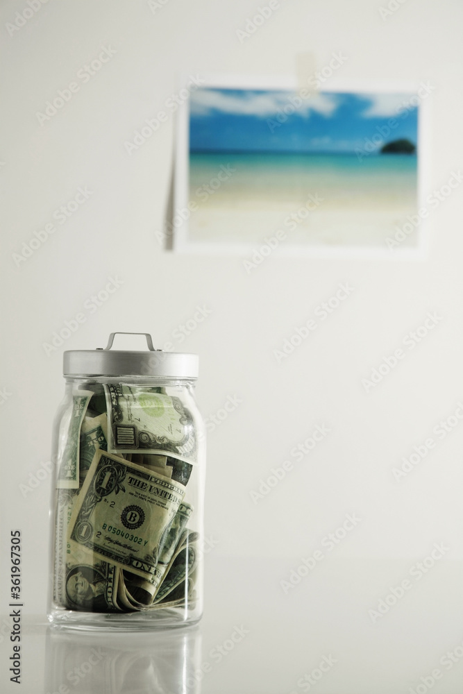 Bank notes in a transparent jar, picture of a beach hanging on the wall ...