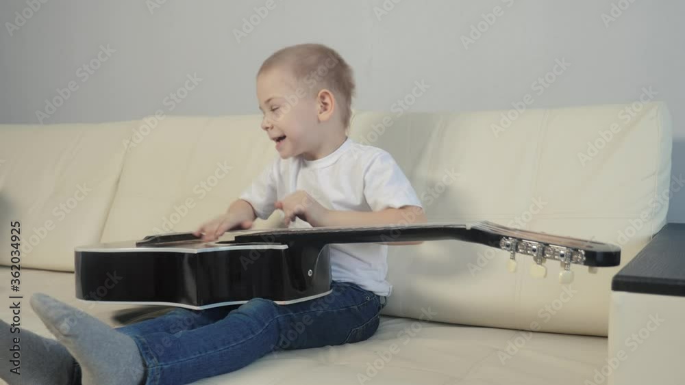 the boy lounges, plays the acoustic guitar. kid makes music play and ...
