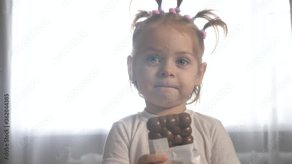 little girl eating chocolate. the child eats sweets. 5 year old blonde ...