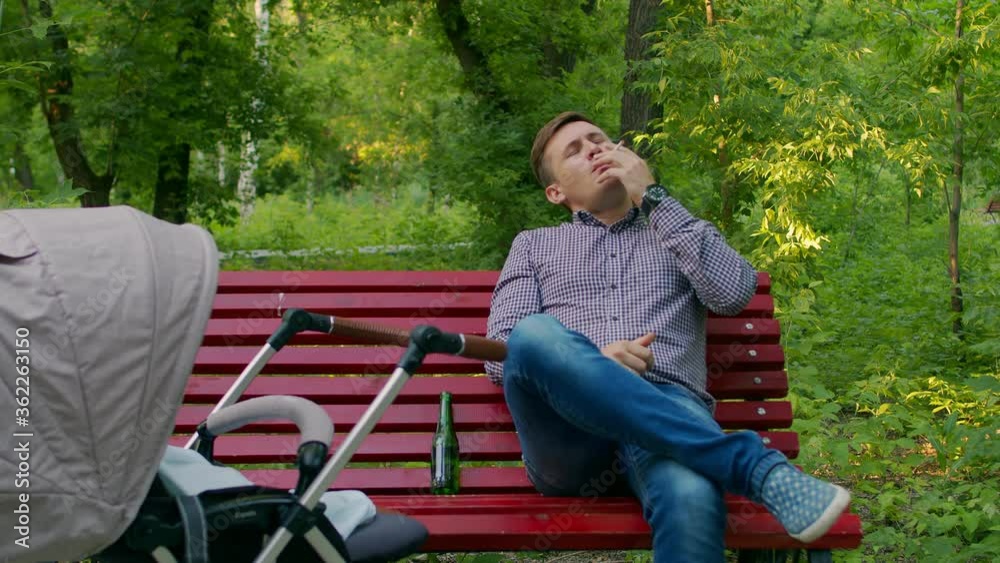 The bad father lights a cigarette, rocks a pram, and drinks beer while ...