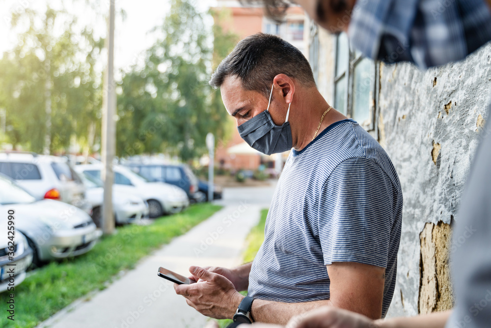 Two men in front of wall using mobile phone app wearing protective mask ...