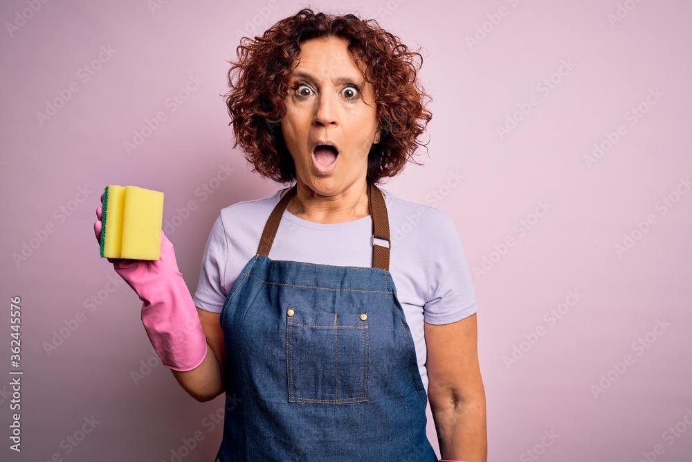 Middle age curly hair woman cleaning doing housework wearing apron and ...