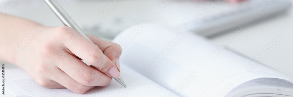 Female hand holding silver pen ready to make note in opened notebook ...