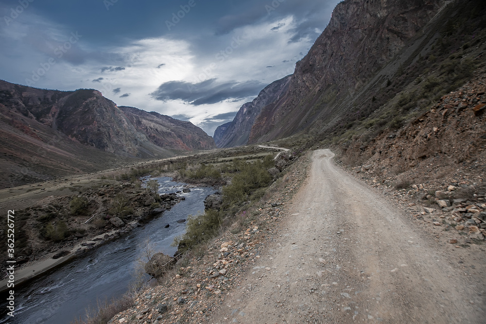 high steep cliffs by the road, a mountain river of blue color flows ...