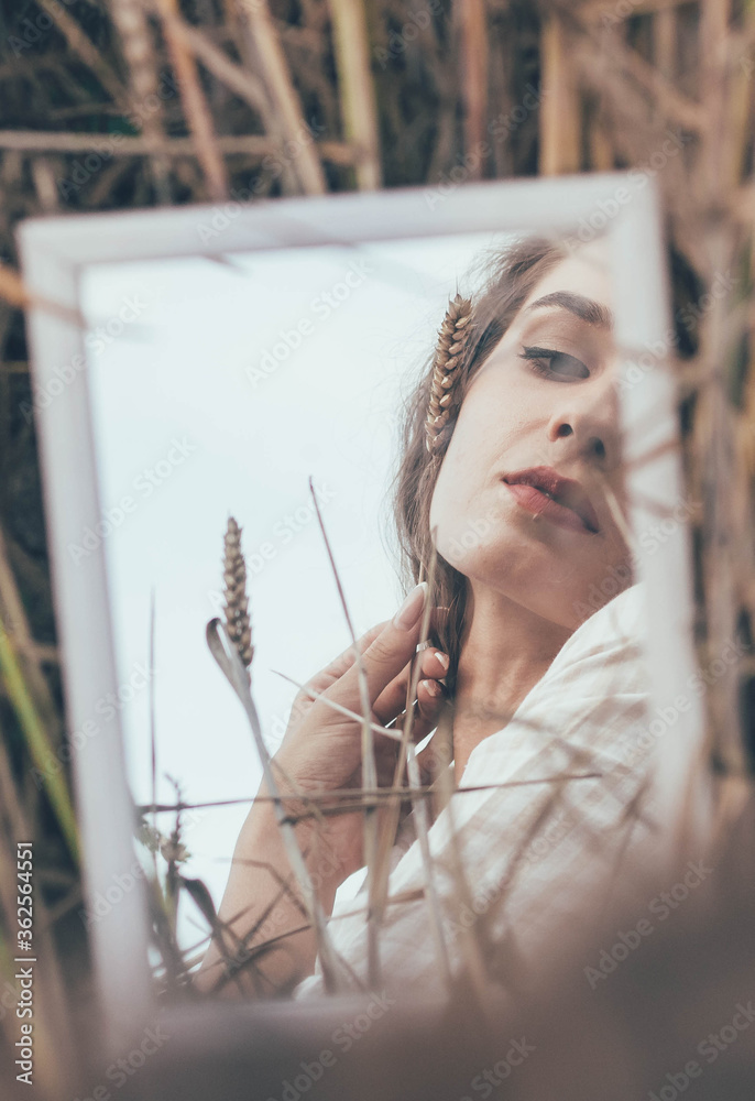reflection of a girl in the mirror, the girl sits in wheat and looks in ...